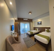 Quarto de hotel com duas camas, uma escrivaninha com cadeira, televisão e janela com cortinas.