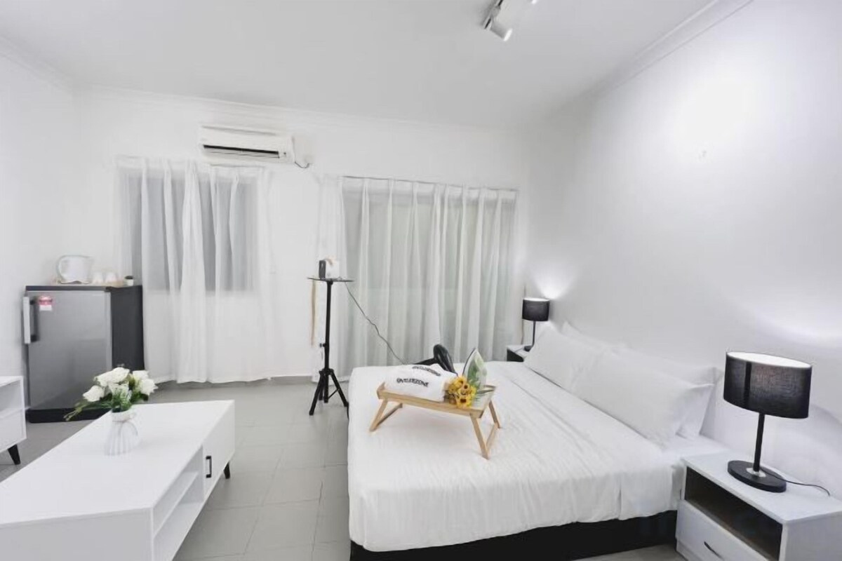 Quarto de hotel com cama, mesa de cabeceira, abajur e escrivaninha com cadeira.