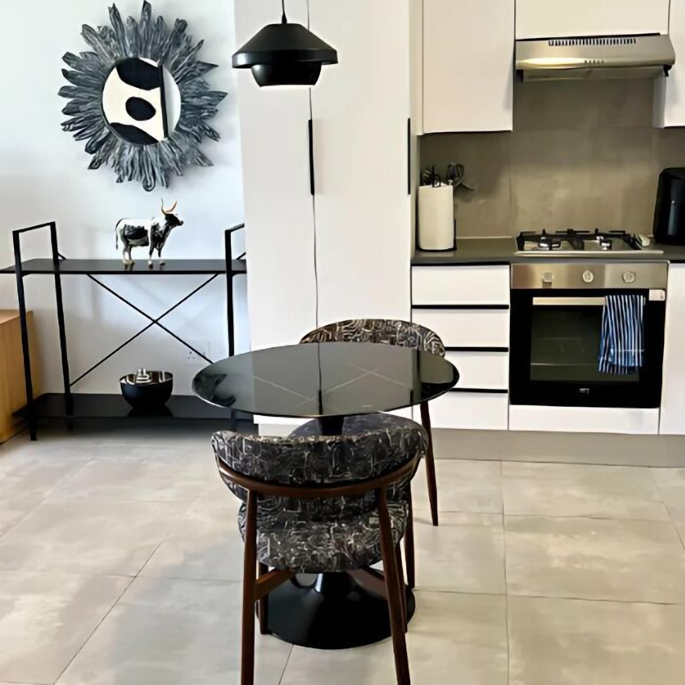 Uma cozinha moderna com fogão a gás, forno e área de refeições com uma mesa redonda e duas cadeiras.