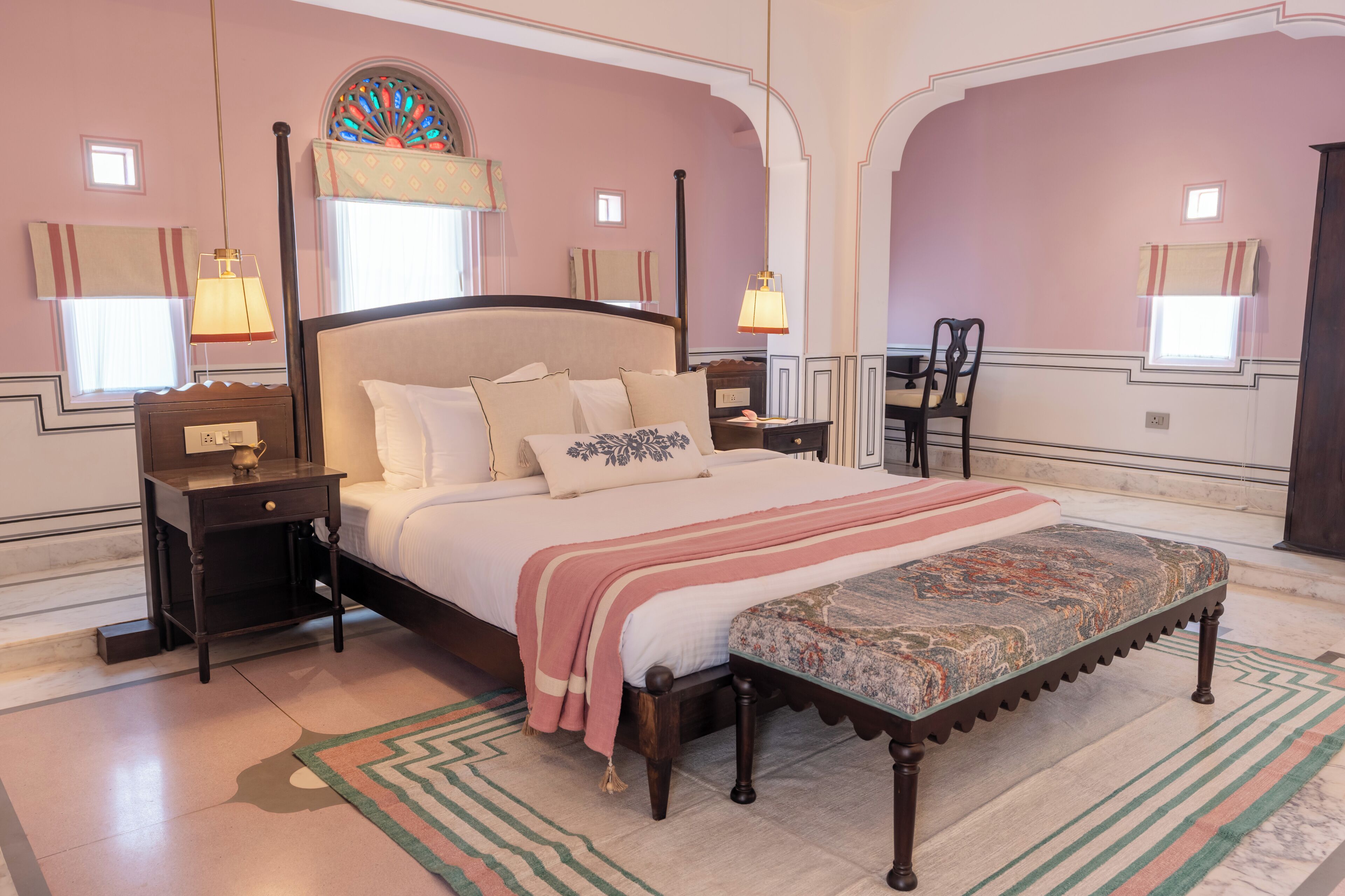Quarto com uma cama grande, duas mesas de cabeceira, um banco e um espelho decorativo.