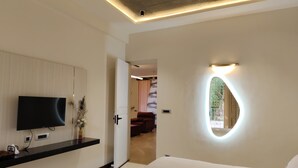 Um quarto moderno com televisão de tela plana, mesa de cabeceira, cama grande e uma janela oval incomum com iluminação embutida.
