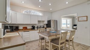 Cozinha com armários brancos, uma mesa de madeira e cadeiras. Há uma janela com vista para o exterior.