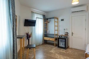 Quarto compacto com cama, escrivaninha, cadeira, televisão, escada, pequeno refrigerador e porta.