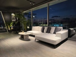 Uma sala de estar moderna com um sofá branco em formato de L, uma mesa de centro redonda e uma área de jantar com cadeiras.