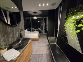 Uma casa de banho moderna com um espelho grande, uma sanita preta, um móvel de banheira em madeira e uma banheira preta.