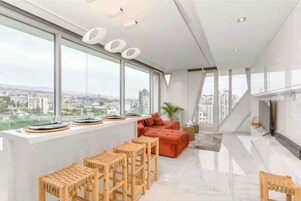 Sala de estar moderna com vista para a cidade, um sofá, banquetas de madeira e uma janela grande.
