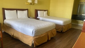 Quarto de hotel com duas camas de solteiro, cabeceiras de madeira e uma pequena cozinha.