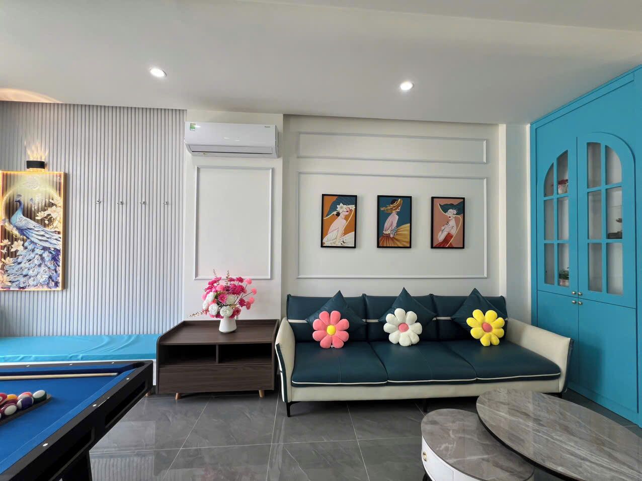 Uma sala de estar com mesa de bilhar, sofá com almofadas em formato de flores e um armário azul.