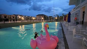 Piscina com um flutuador em formato de flamingo rosa, rodeada por espreguiçadeiras e um edifício com fachada branca.