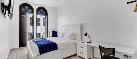 Quarto com cama, mesa de cabeceira, escrivaninha, cadeira e televisão na parede.