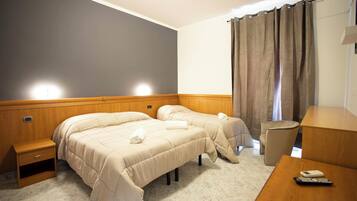 Quarto de hotel com duas camas, uma mesa de cabeceira de madeira, uma mesinha e uma cadeira.