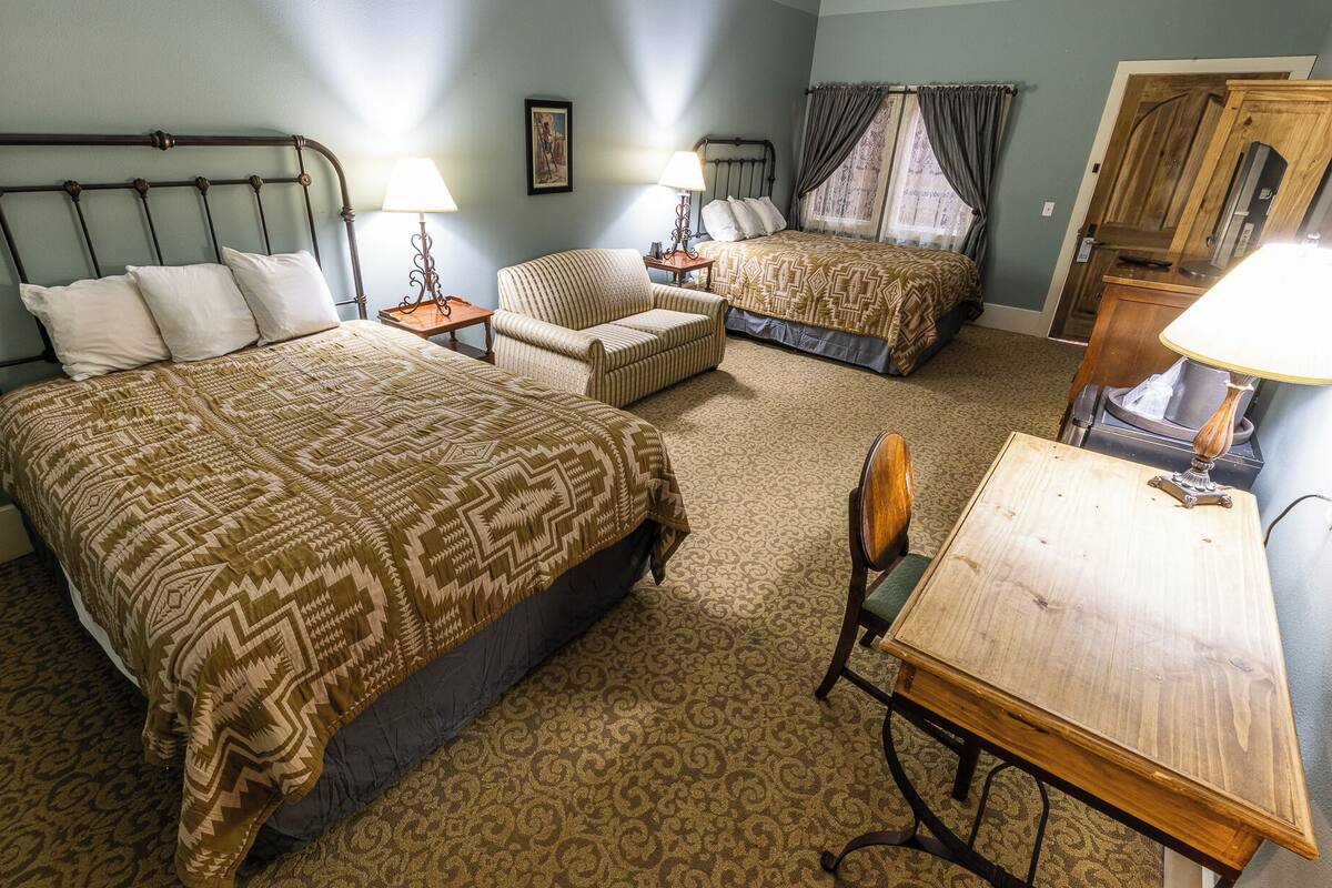 Quarto com duas camas, uma cadeira, uma mesa e um abajur.