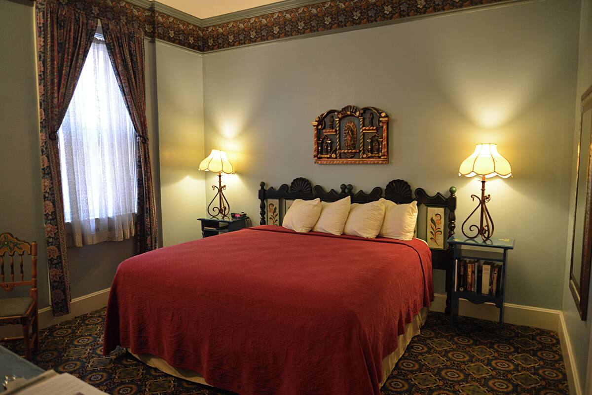 Quarto com uma cama grande, duas mesas de cabeceira com luminárias, um espelho decorativo e um tapete estampado.