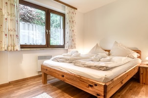 Uma cama de madeira com lençóis brancos, uma janela com cortinas florais e uma mesa de cabeceira de madeira.