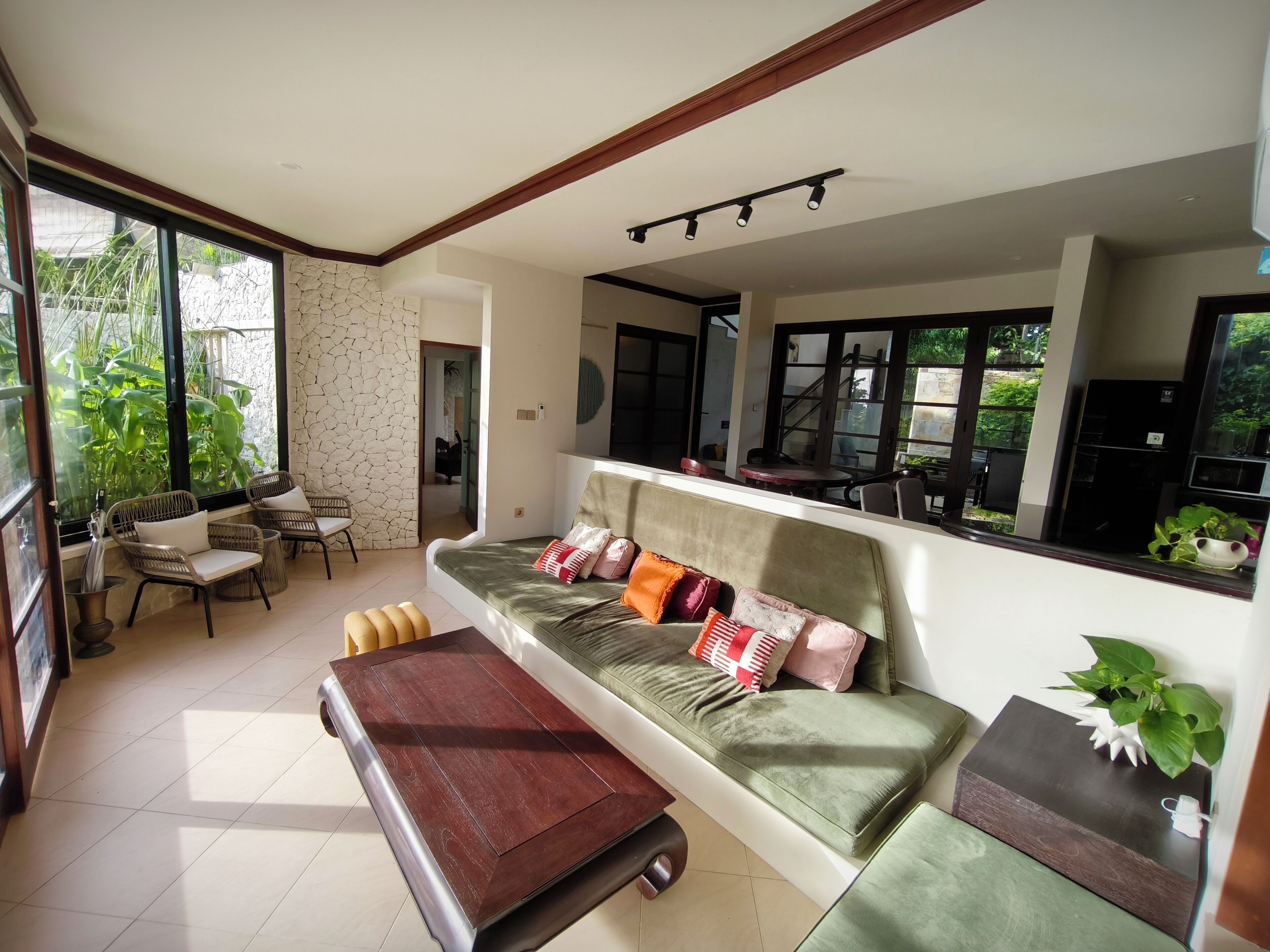 Uma sala de estar moderna com sofá, mesa de centro e cadeiras. Há uma janela grande com plantas do lado de fora.