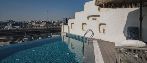 Uma piscina no terraço com água azul cristalina, um telhado de palha e vista para a paisagem urbana.