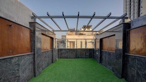 Terraço no telhado com grama sintética, pérgola e vista dos edifícios ao redor.