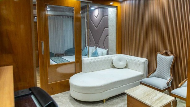 Quarto moderno com sofá branco, parede de destaque em madeira e porta de armário com espelho.