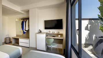 Quarto de hotel com duas camas, uma escrivaninha com televisão, um guarda-roupa e um pequeno frigorífico.