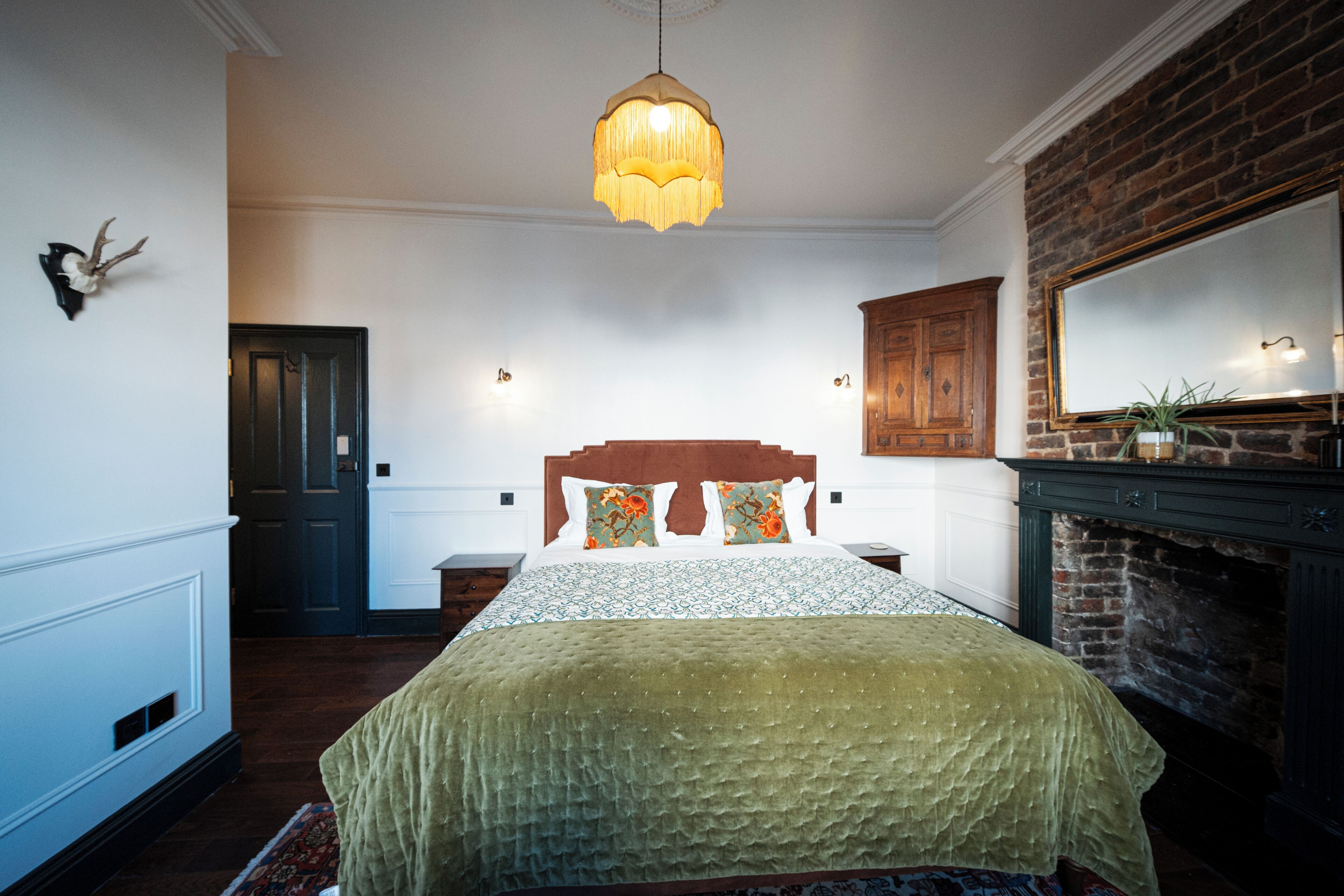 Um quarto com cama, cabeceira de madeira, luminária pendente, lareira de tijolos e um espelho na parede.