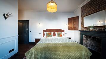 Um quarto com cama, cabeceira de madeira, luminária pendente, lareira de tijolos e um espelho na parede.