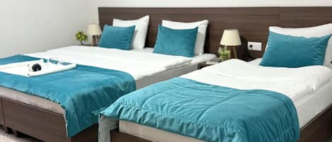 Duas camas de solteiro com roupa de cama verde-água, cabeceiras de madeira e abajures laterais.
