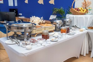Uma mesa de buffet com diversos alimentos e recipientes, incluindo pão, doces e acompanhamentos.