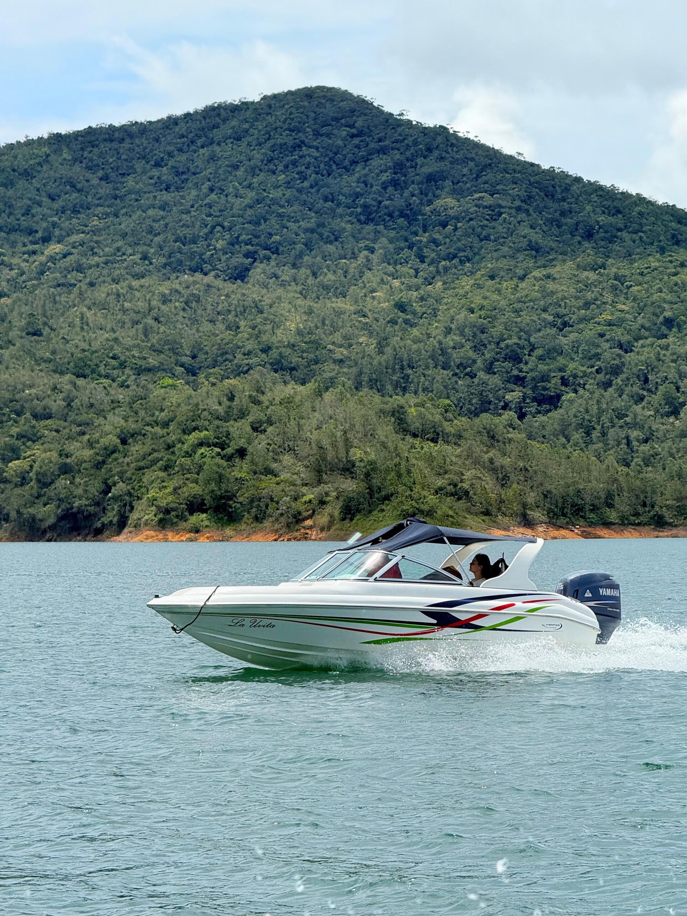 Um barco a motor rápido em um lago, com uma colina arborizada ao fundo.