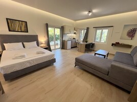 Quarto de hotel moderno com uma cama grande, sofá, escrivaninha e cozinha compacta.