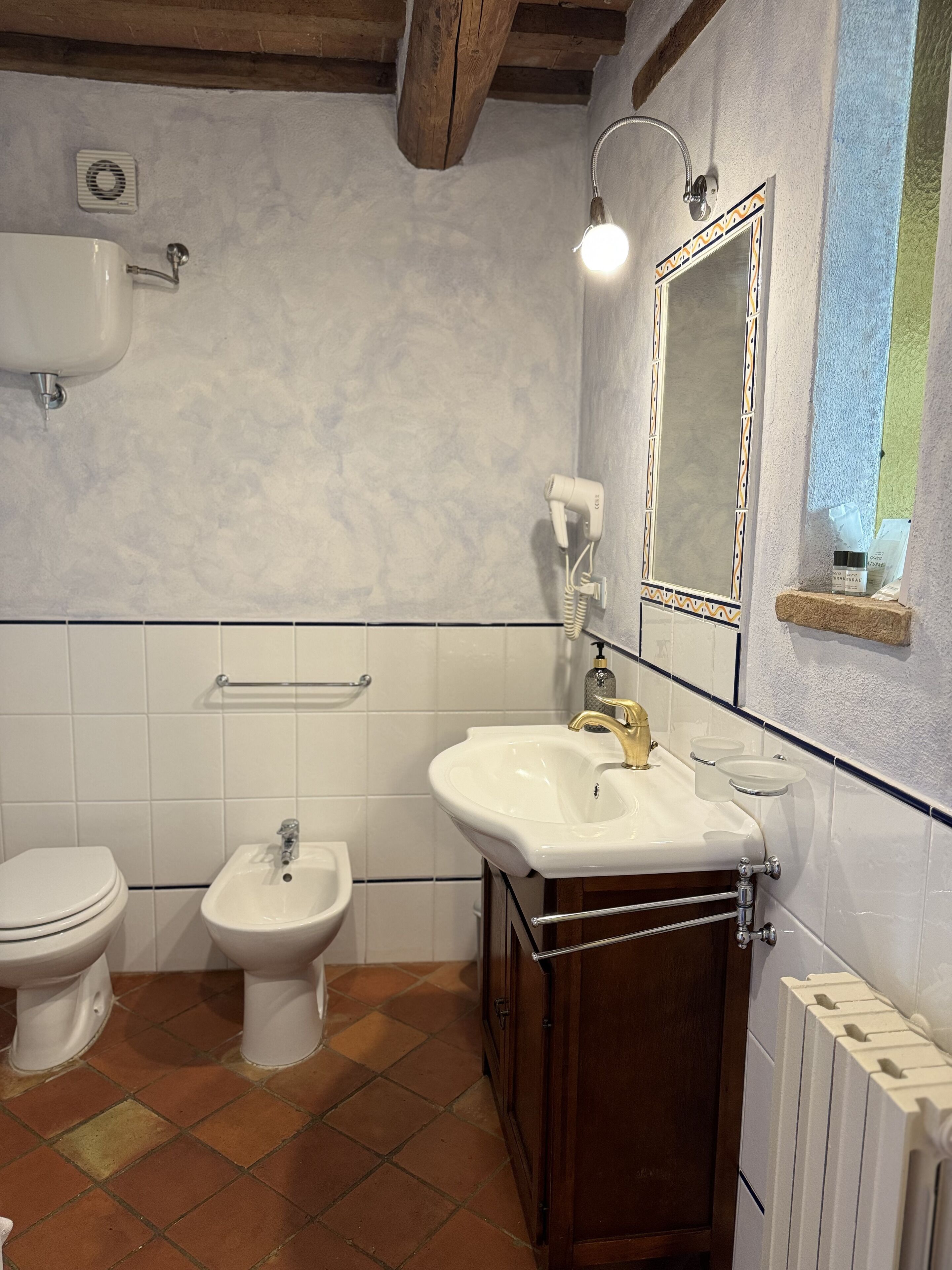 Um banheiro com pia branca, bidê, vaso sanitário e espelho com moldura decorativa.