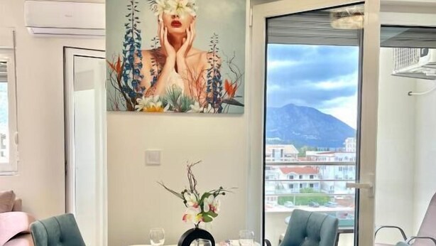 Uma sala de jantar com uma mesa redonda, quatro cadeiras azuis, um vaso com flores e um quadro na parede.