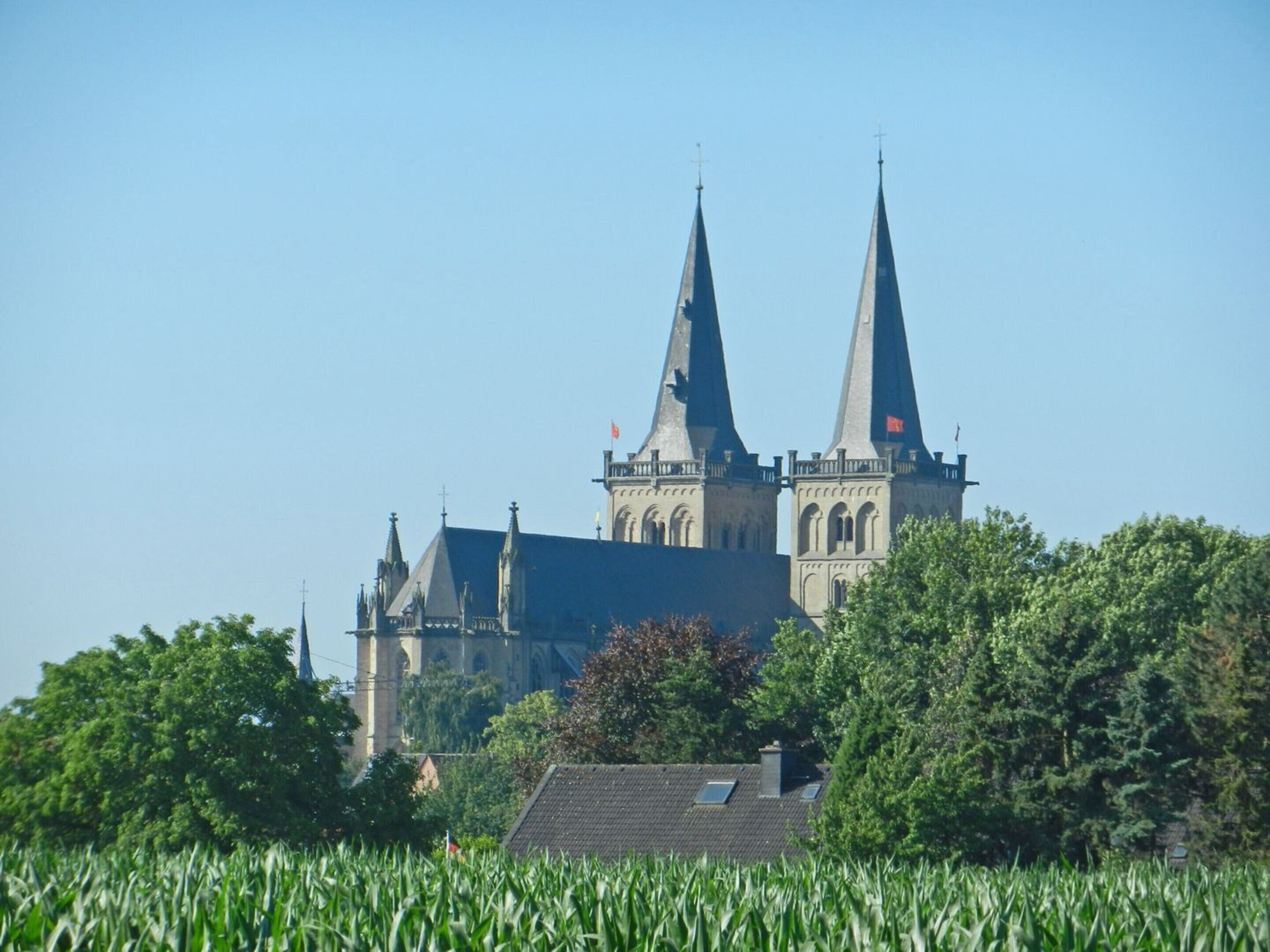 Um edifício histórico com duas torres imponentes, rodeado por vegetação exuberante e um campo.