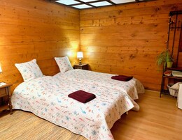 Um quarto aconchegante com paredes de madeira, uma cama com roupa de cama florida, uma mesa de cabeceira com abajur e uma pequena planta.