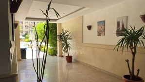 Um corredor amplo com plantas em vasos, piso ladrilhado e obras de arte nas paredes.