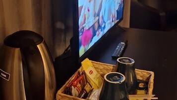 Uma televisão sobre uma mesa com petiscos e uma chaleira.