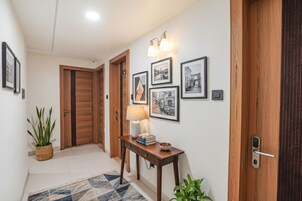 Um corredor com portas de madeira, uma luminária na parede e quadros emoldurados.