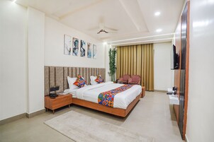 Quarto de hotel moderno com uma cama grande, mesa de cabeceira, escrivaninha, cadeira, televisão e uma planta.