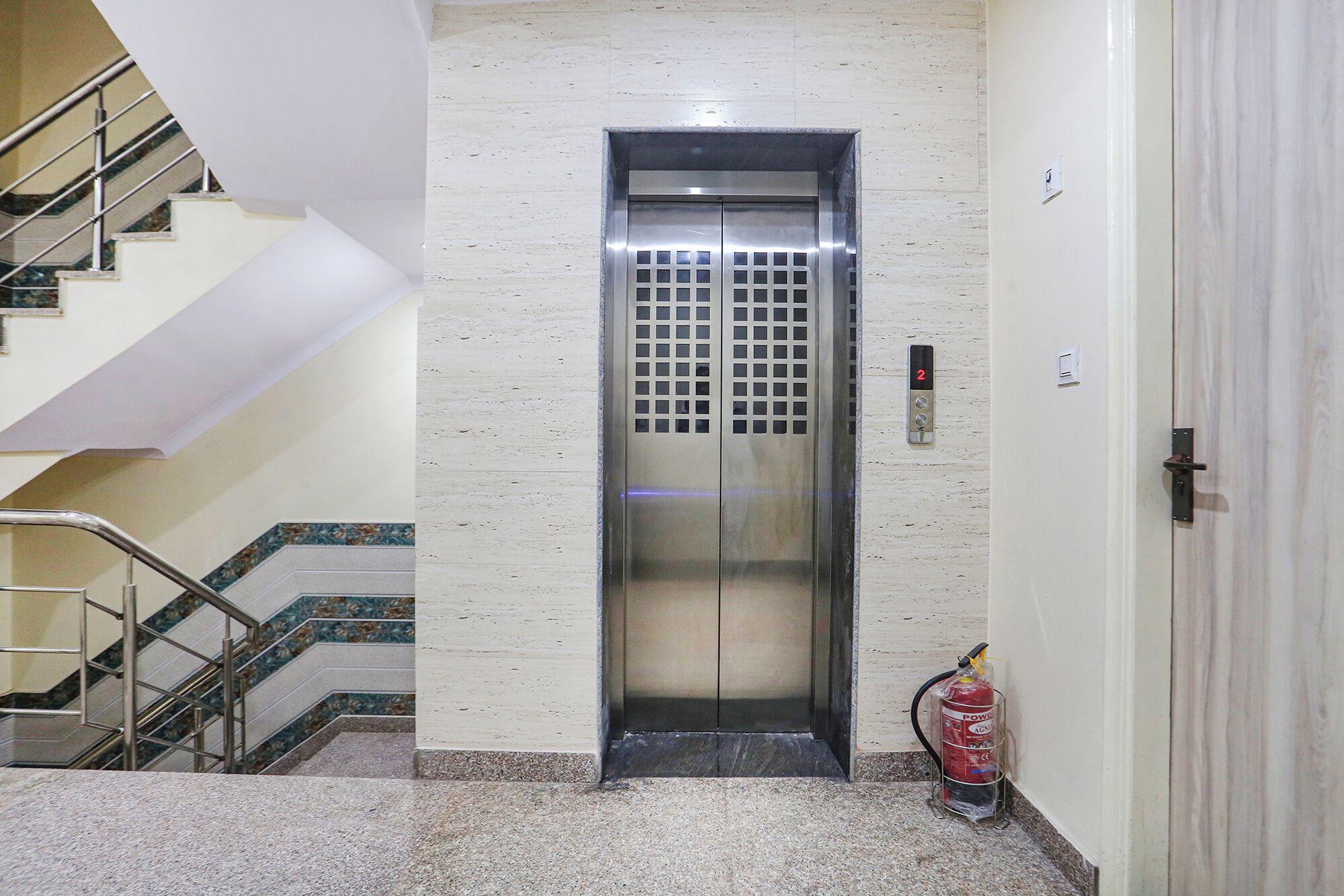 Um elevador com painel de comando e um extintor de incêndio nas proximidades.
