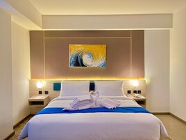 Quarto de hotel com uma cama grande, duas mesas de cabeceira, um quadro pendurado na parede e uma parede com detalhes em azul.