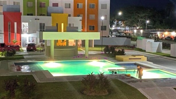 Um hotel com vários andares, área de piscina, rodeado por vegetação e iluminado por iluminação pública.