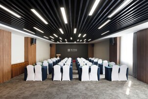 Uma sala de conferências com mesas e cadeiras dispostas em fileiras, uma tela de projeção e uma parede de detalhes em madeira.