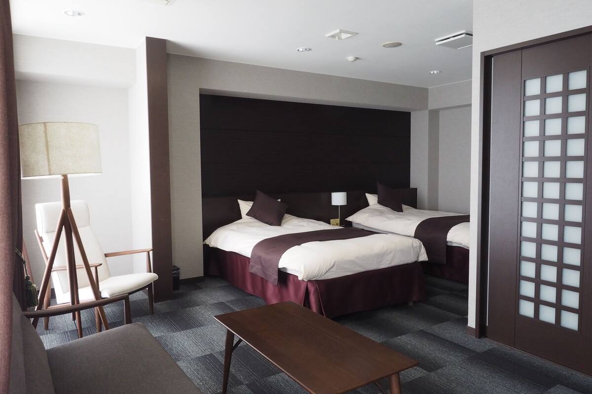 Quarto de hotel com duas camas, uma mesa, uma cadeira e um abajur.