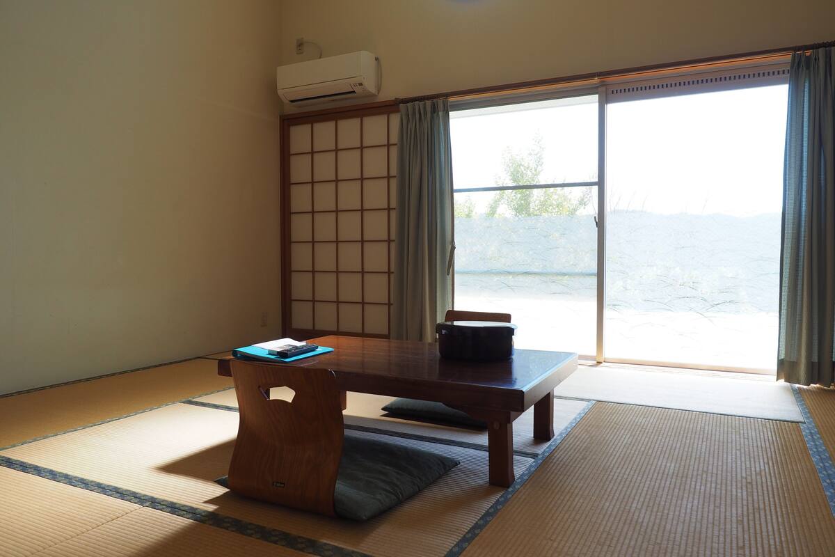 Quarto japonês tradicional com tatames, uma mesa de madeira e uma porta deslizante com vista para a água.