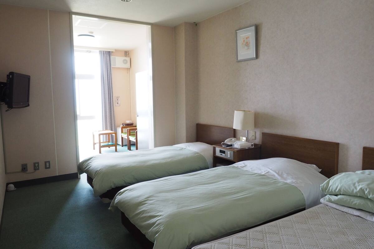 Quarto de hotel com duas camas, uma escrivaninha com abajur, televisão e porta para uma varanda.