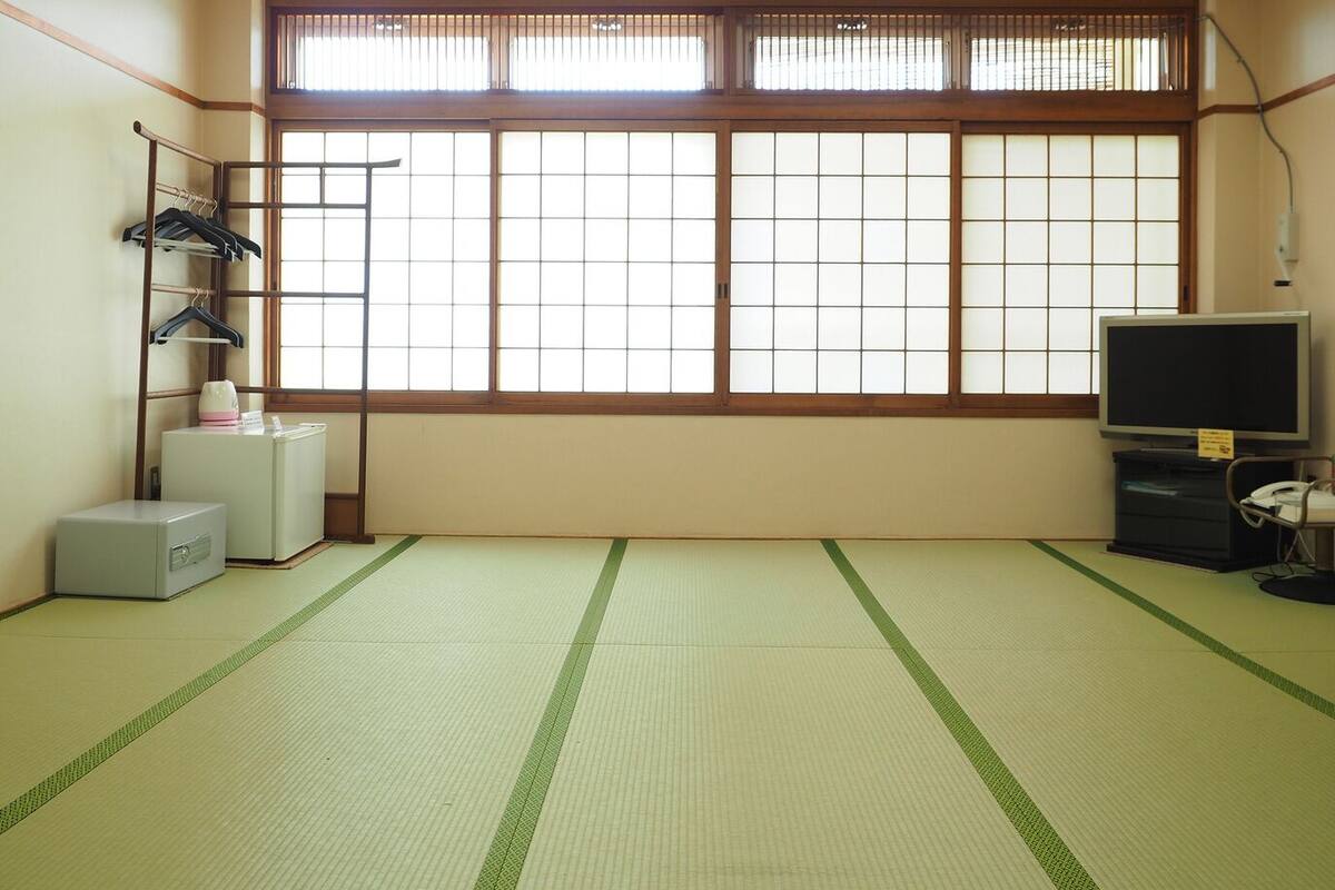 Quarto com piso de tatame, televisão, escrivaninha com computador e janela com tradicionais biombos shoji.