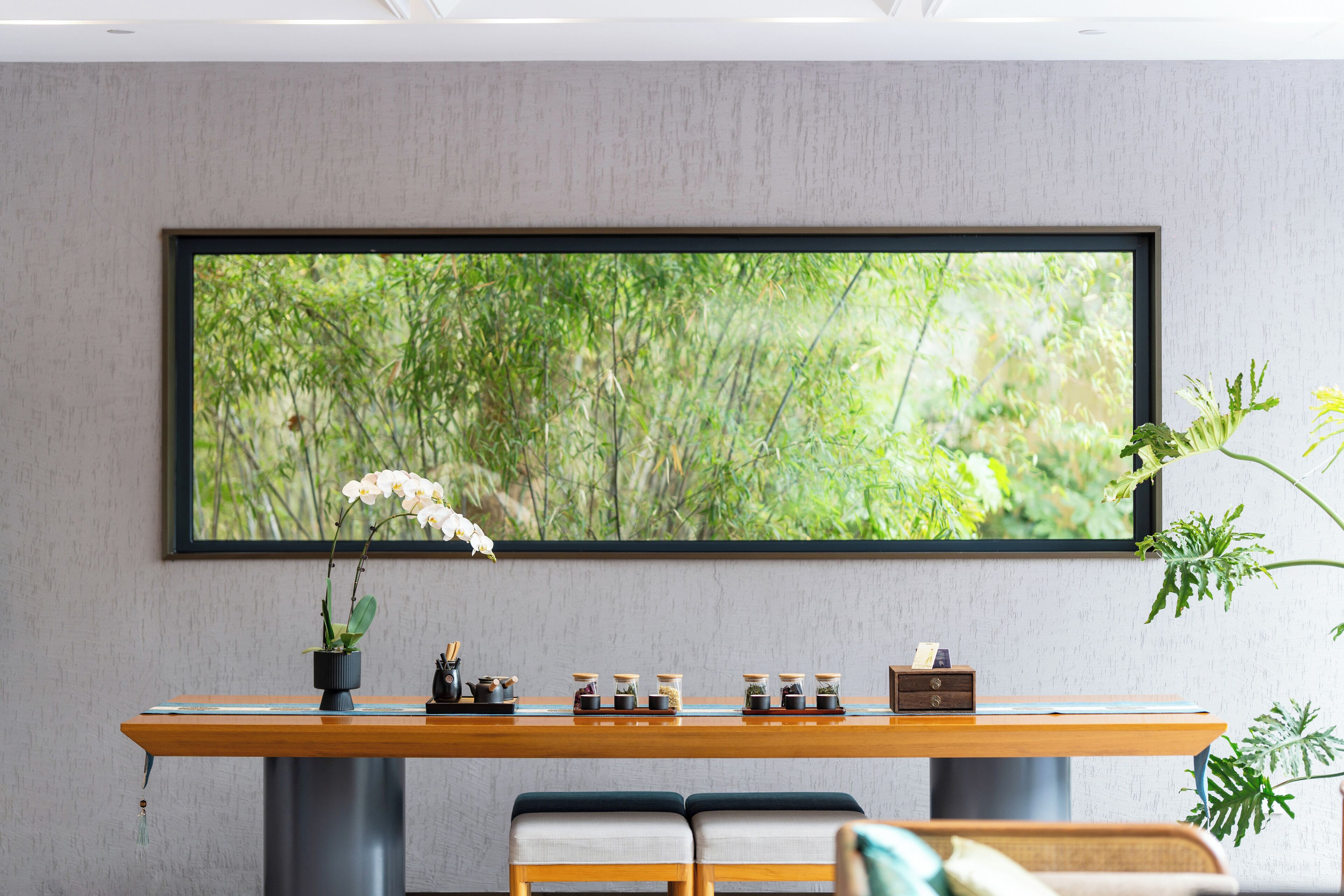 Quarto moderno com uma janela grande, uma escrivaninha de madeira, duas cadeiras e uma orquídea em vaso.