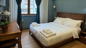 Quarto de hotel com cama, escrivaninha, luminária e vista para a cidade pela janela.