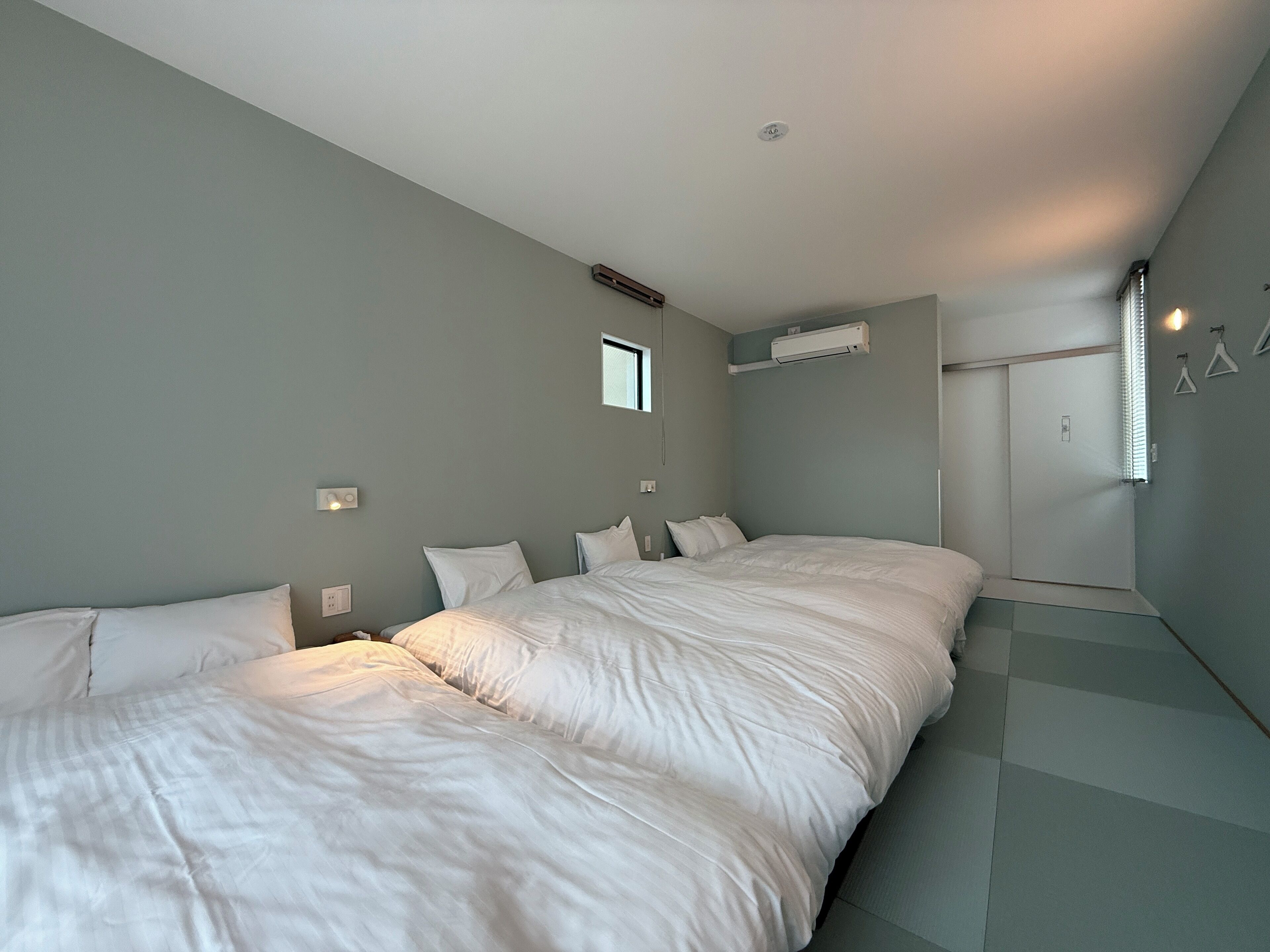 Quarto moderno com duas camas grandes, roupeiro embutido e janela com persianas.