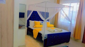 Quarto com cama sob um dossel, mesa de cabeceira e espelho.