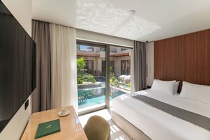 Quarto de hotel com uma cama, uma escrivaninha com cadeira, uma televisão e vista para uma piscina ao ar livre e jardim.